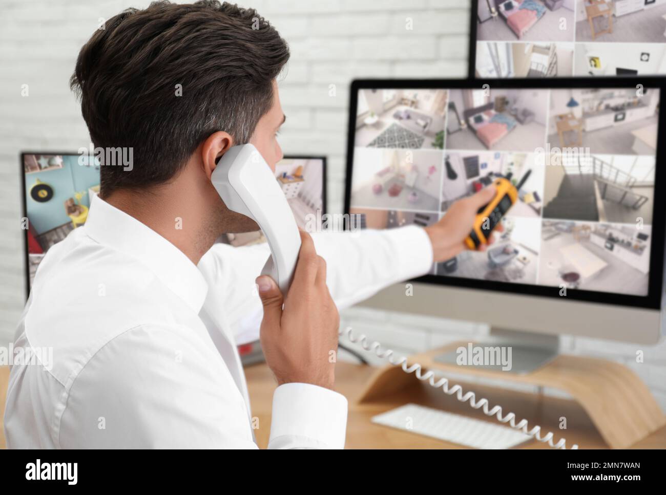 Male security guard talking by telephone near monitors at workplace ...