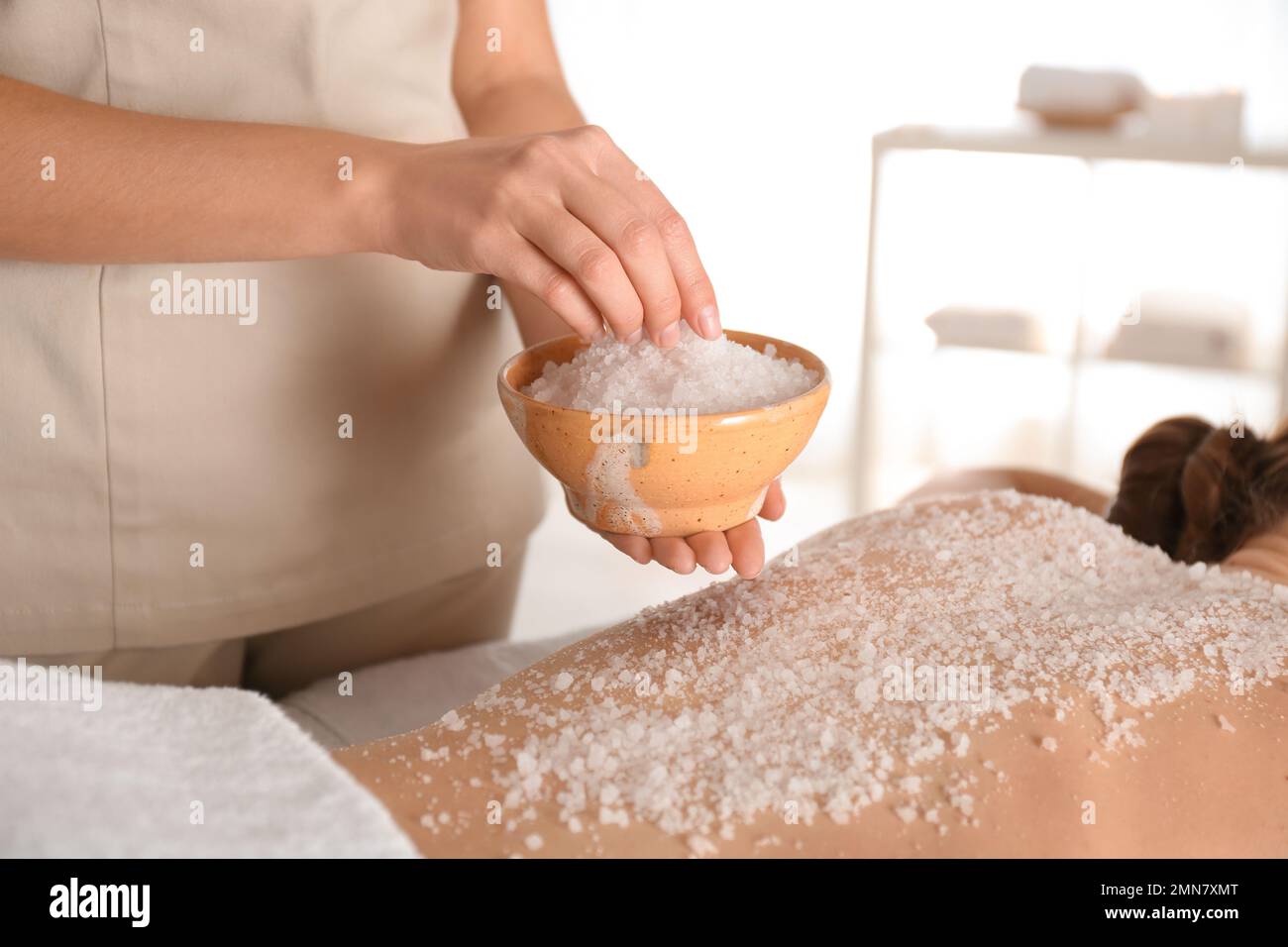 Young woman having body scrubbing procedure with sea salt in spa salon ...