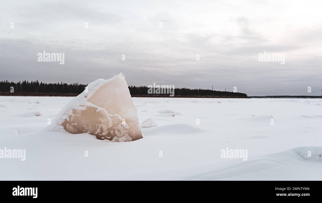 A triangular piece of ice sticks out of the snow on the river in the ...