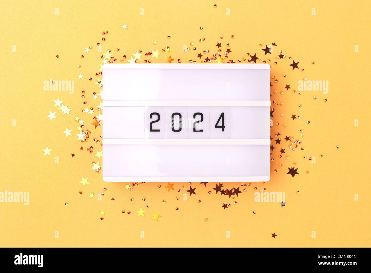 Lightbox with 2024 numbers and shiny stars confetti on a gold colored ...