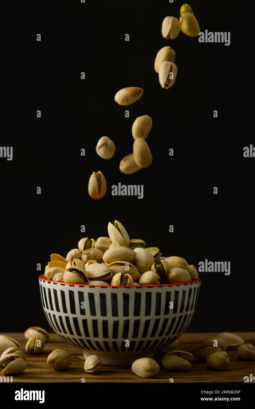 A bunch of pistachios falling on a bowl full of pistachios on a wooden ...