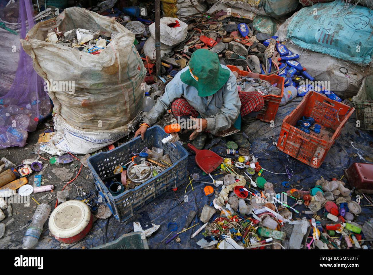 A rag picker segregates plastic waste for recycling at a junkyard in ...