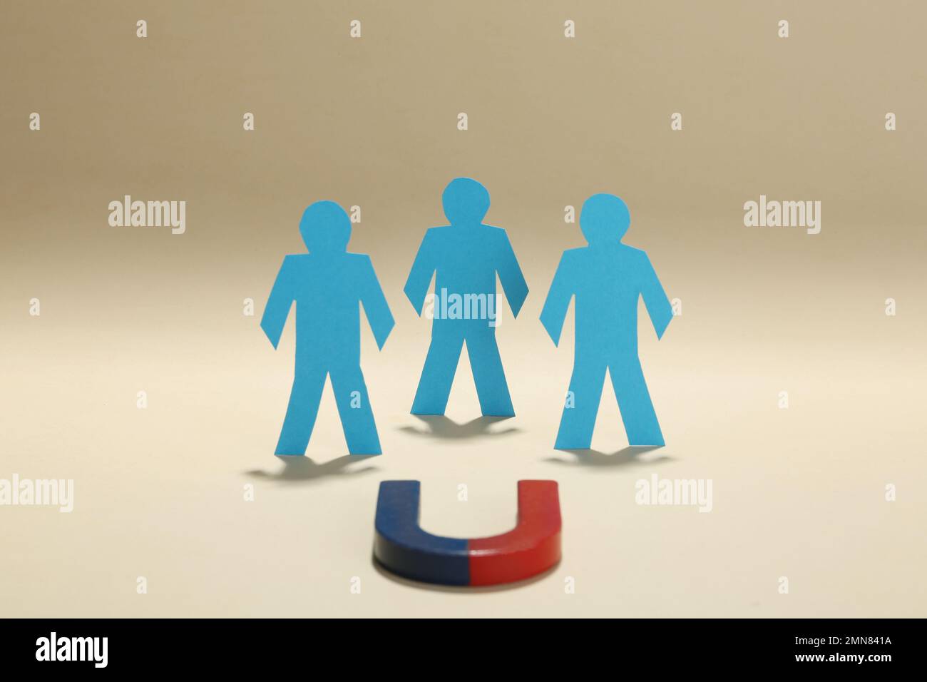 Magnet attracting paper people on beige background Stock Photo - Alamy