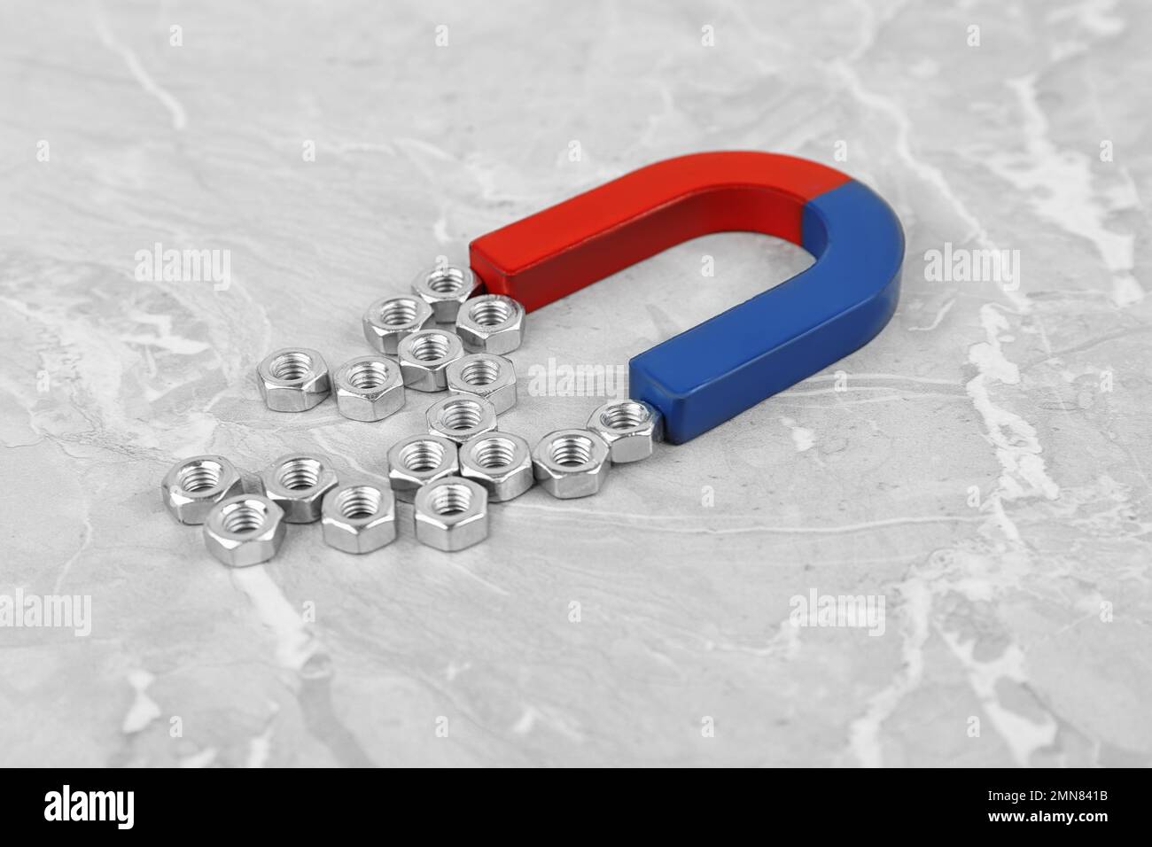Magnet attracting metal nuts on grey marble table Stock Photo - Alamy