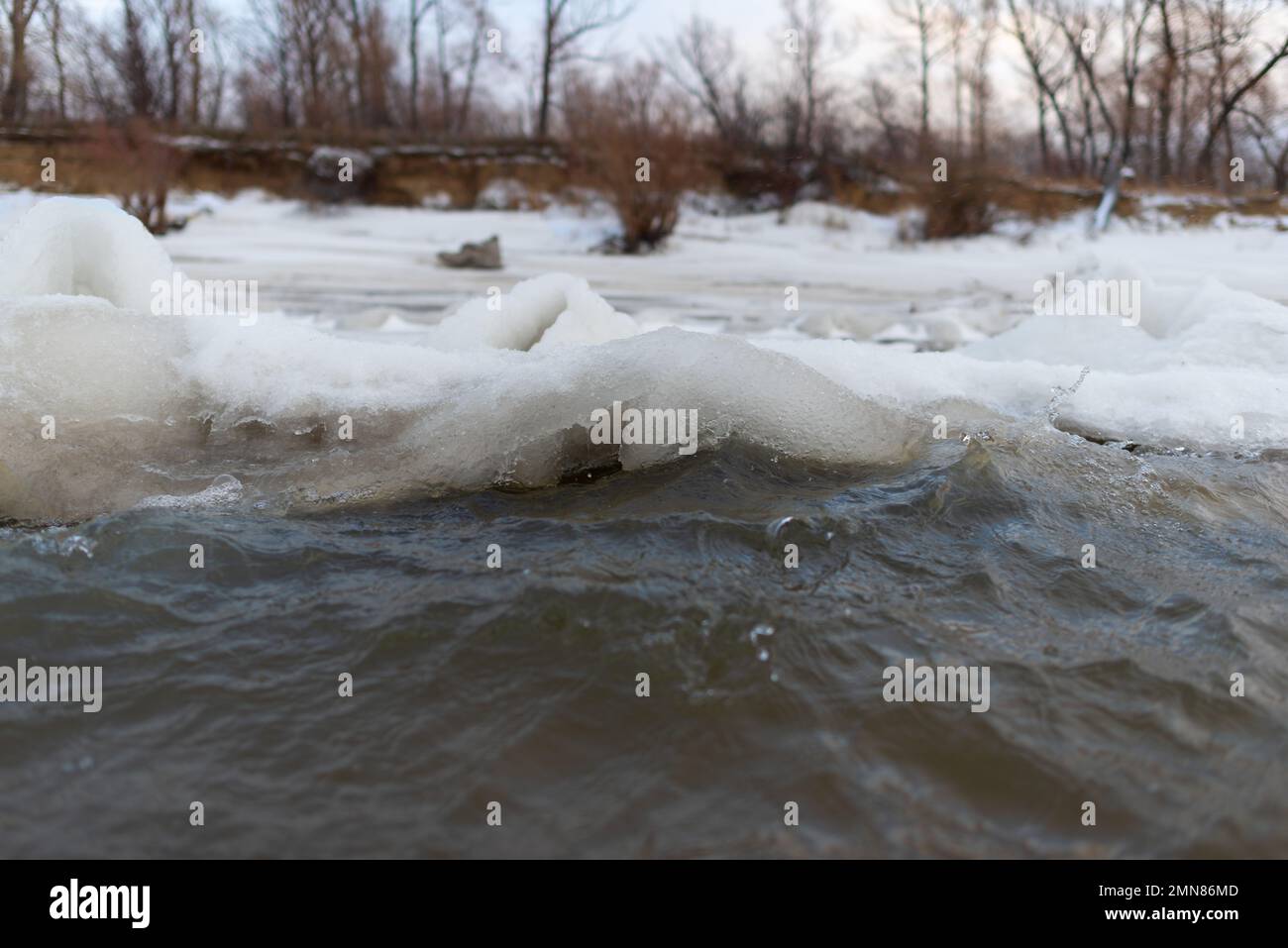 The first ice with snow on the bank of the river rises in waves from ...