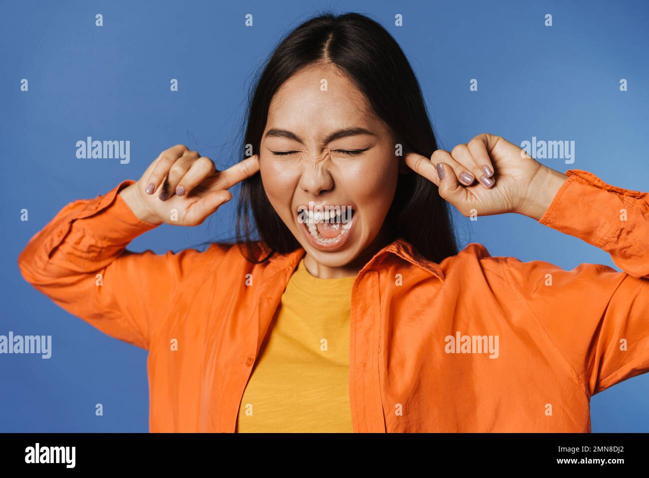 Young asian excited woman wearing shirt screaming and plugging her ears ...