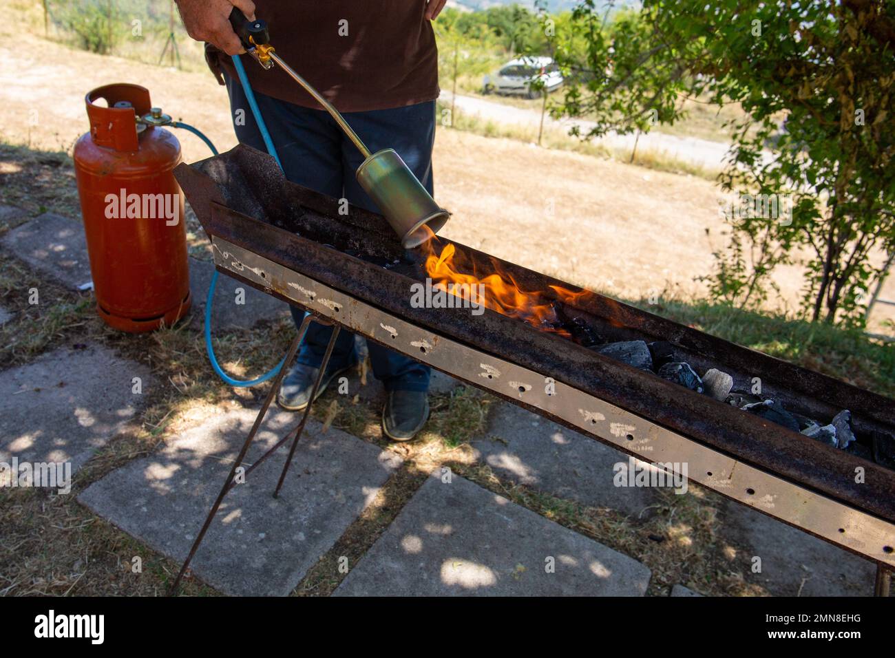 A man with a gas blowtorch ignites charcoal in a barbeque. A man lights ...