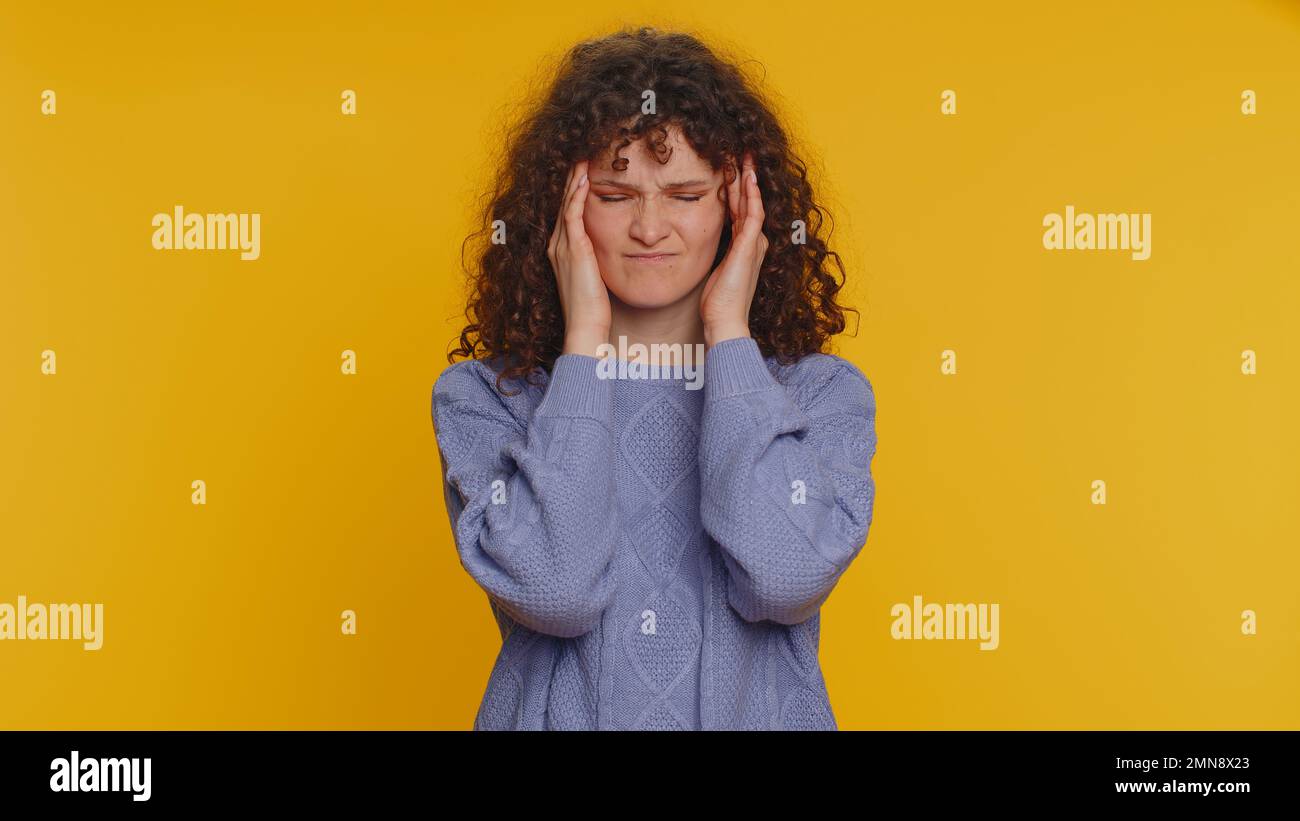 Hipster young curly haired woman in sweater rubbing temples to cure ...