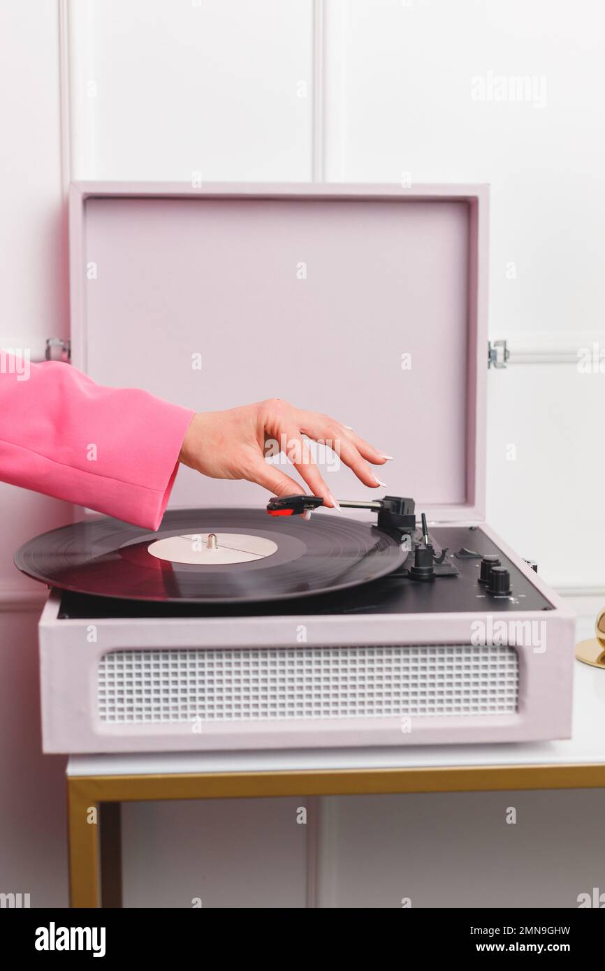 Female hand in pink blazer starting vinyl turntable at the home party ...