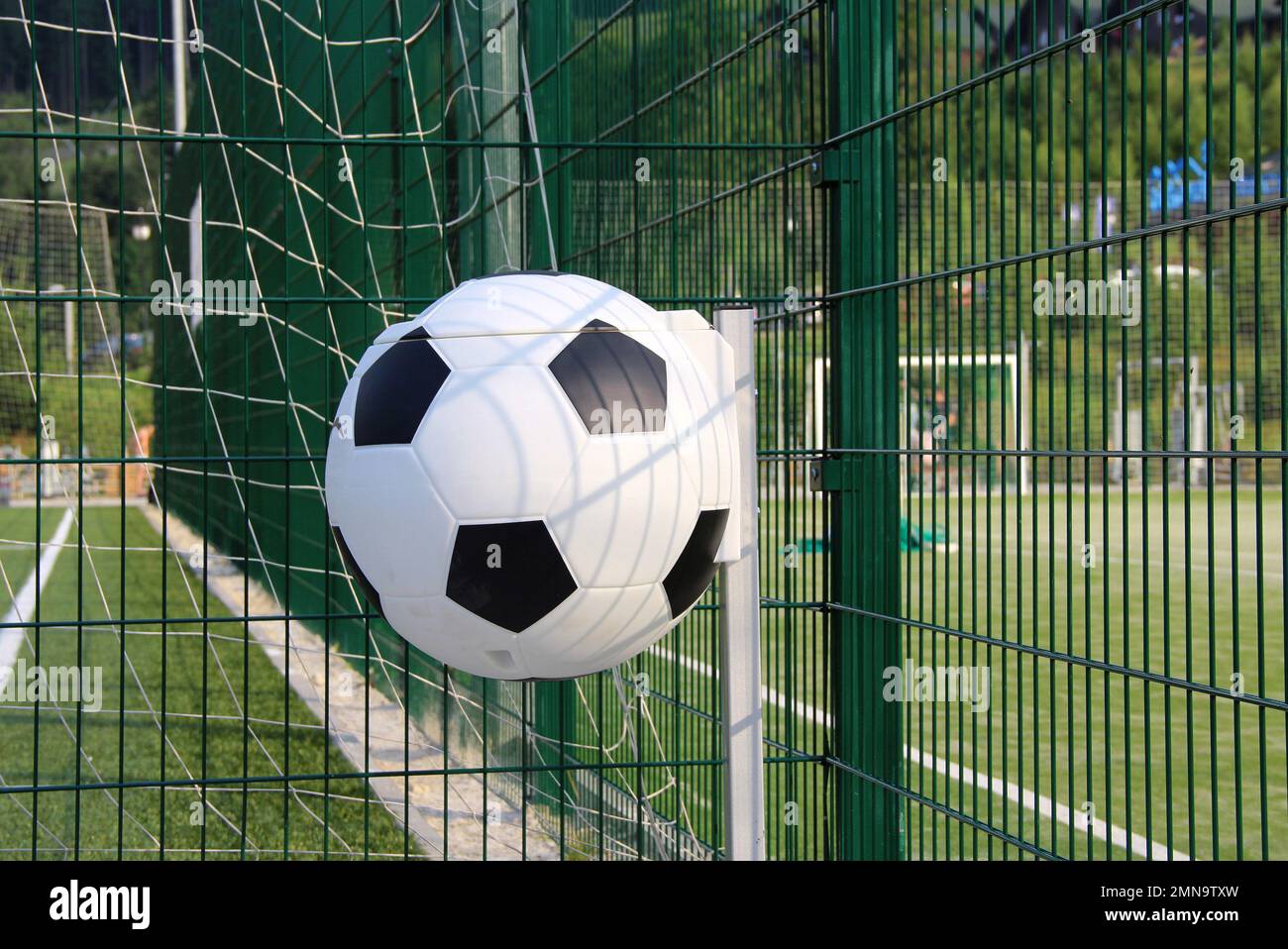 Plastic garbage can in the shape of a soccer ball near fenced football ...