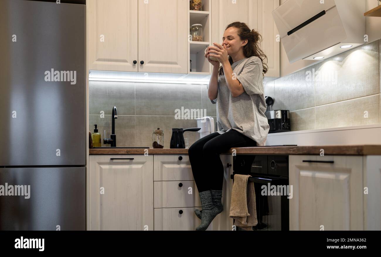 Woman sitting on kitchen workplace and drinking coffee in morning Stock ...
