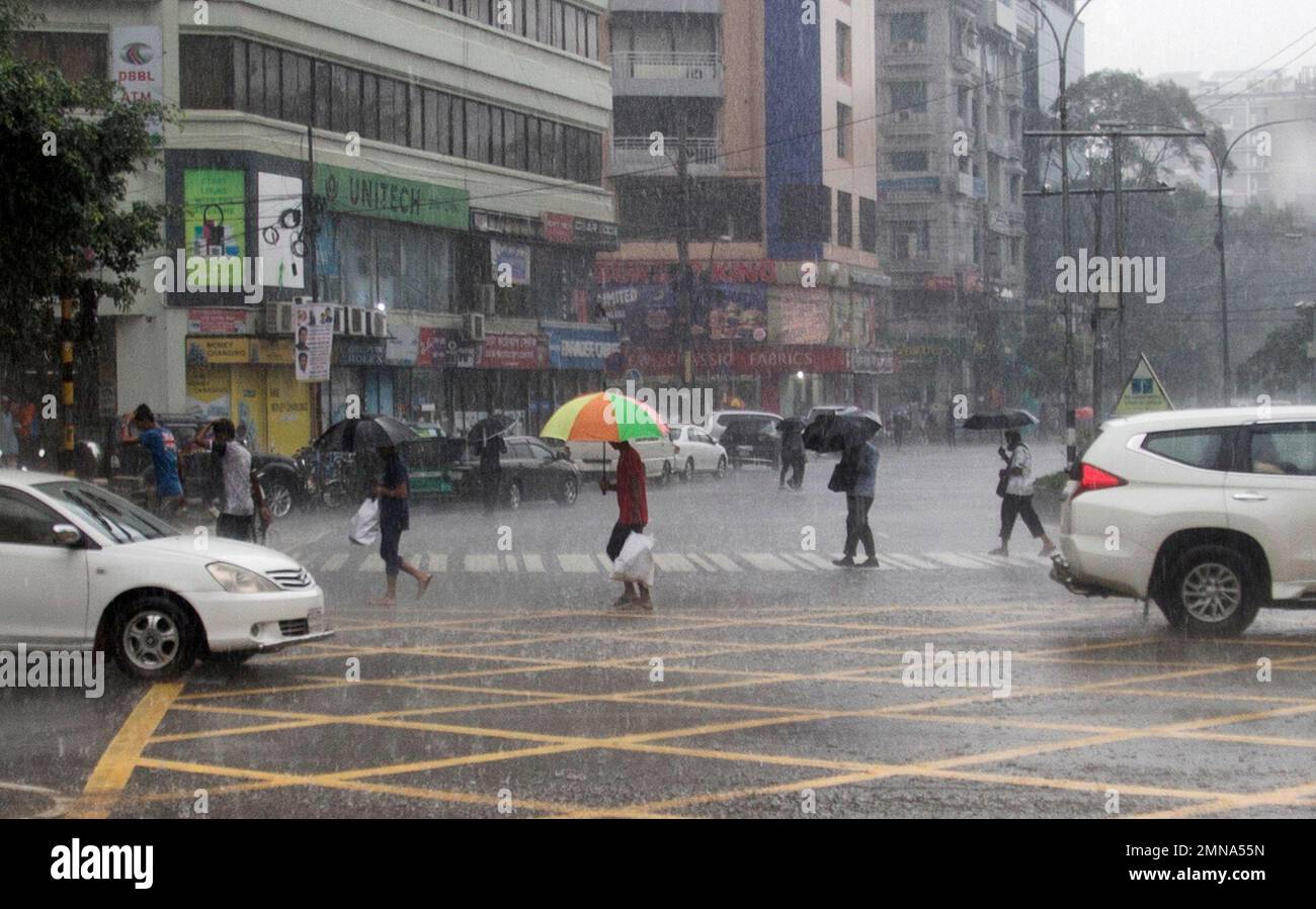 Bangladeshis hold umbrellas and cross a street in the rain in Dhaka ...