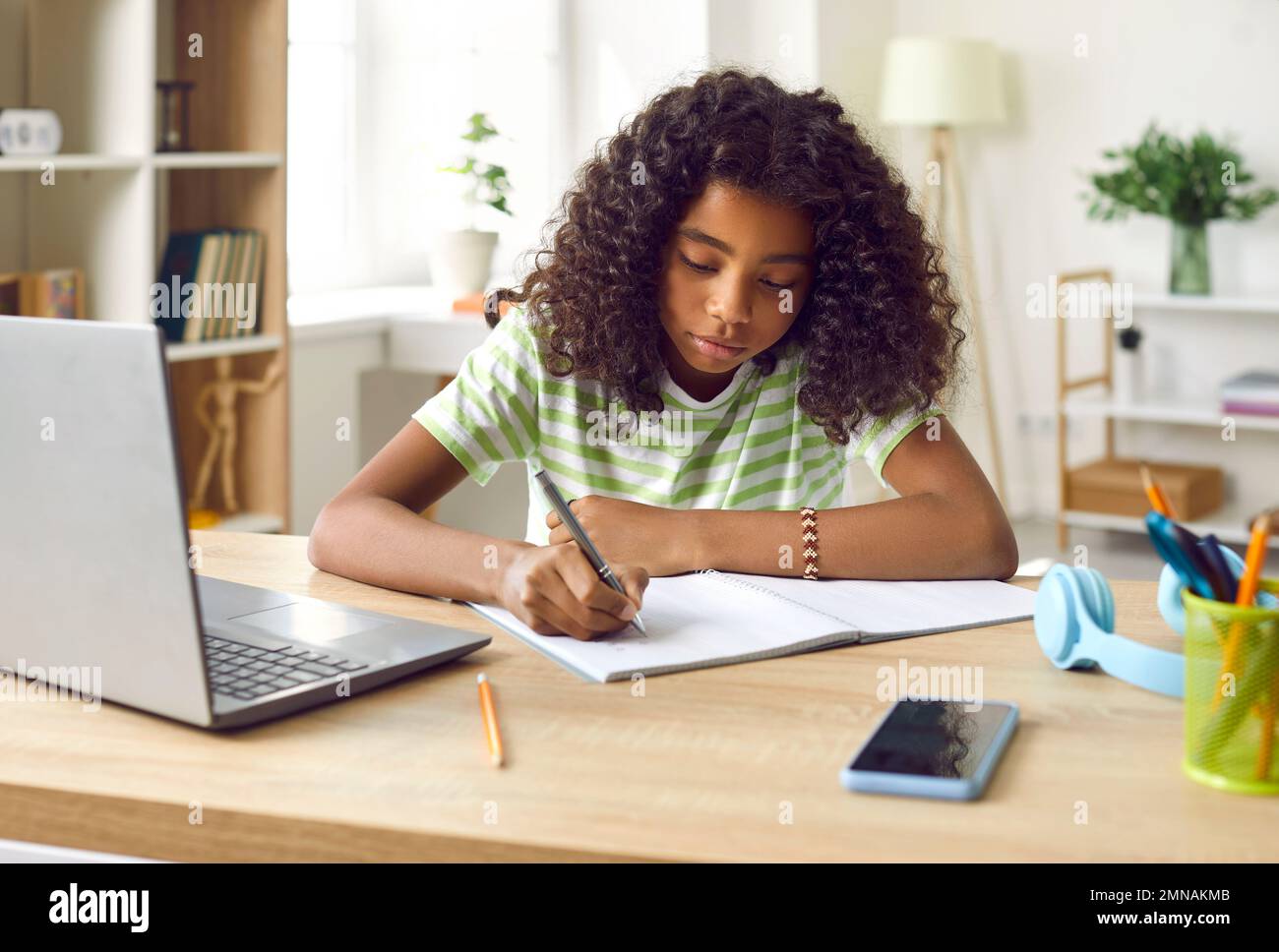 School girl sitting at her desk at home, doing homework, writing essay ...