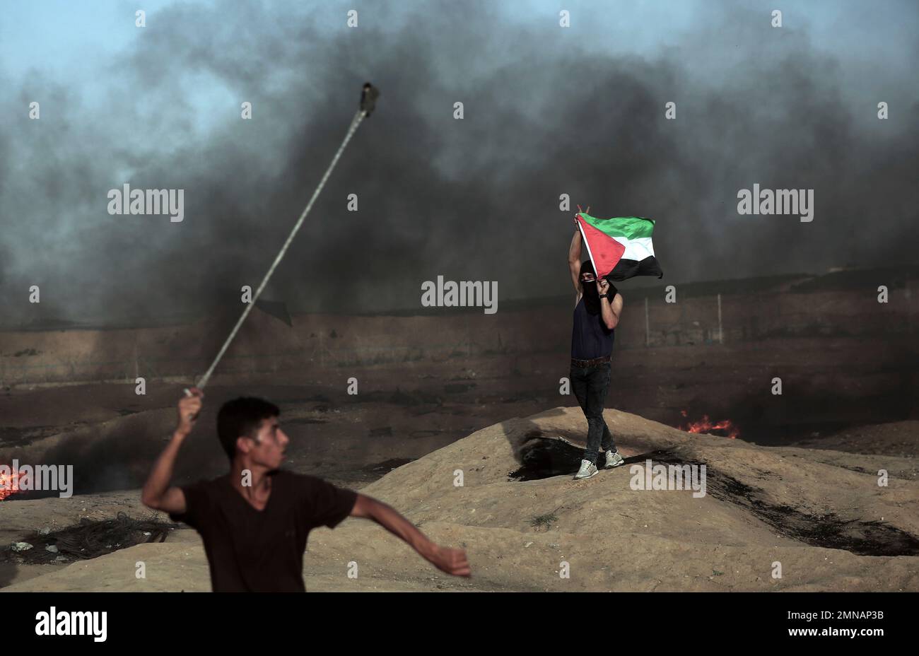 A protester hurls stones at Israeli troops as another holds a ...