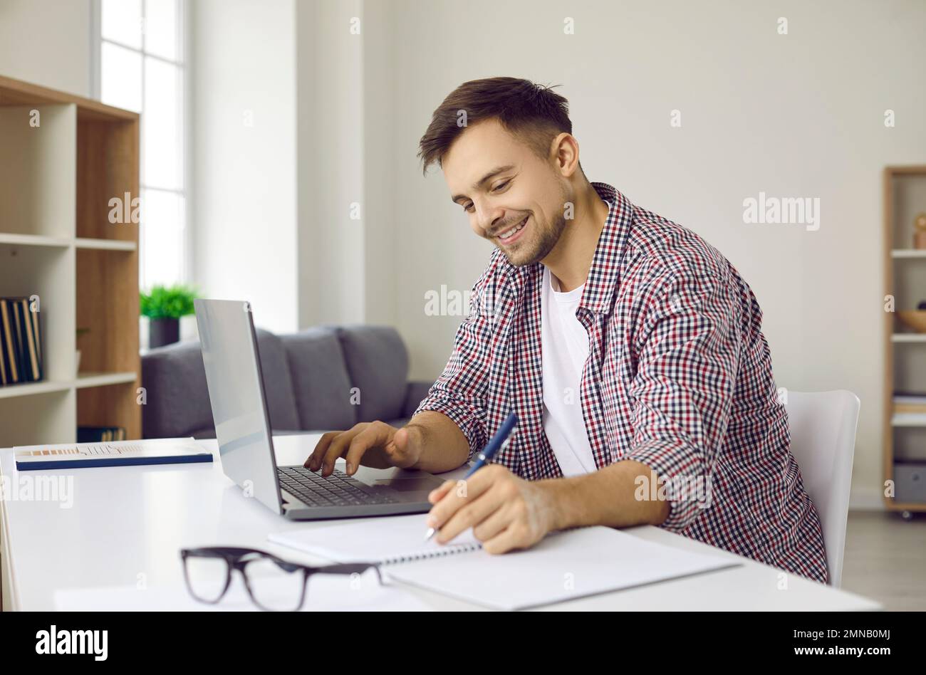 Happy student sitting at desk, using his modern laptop computer and ...