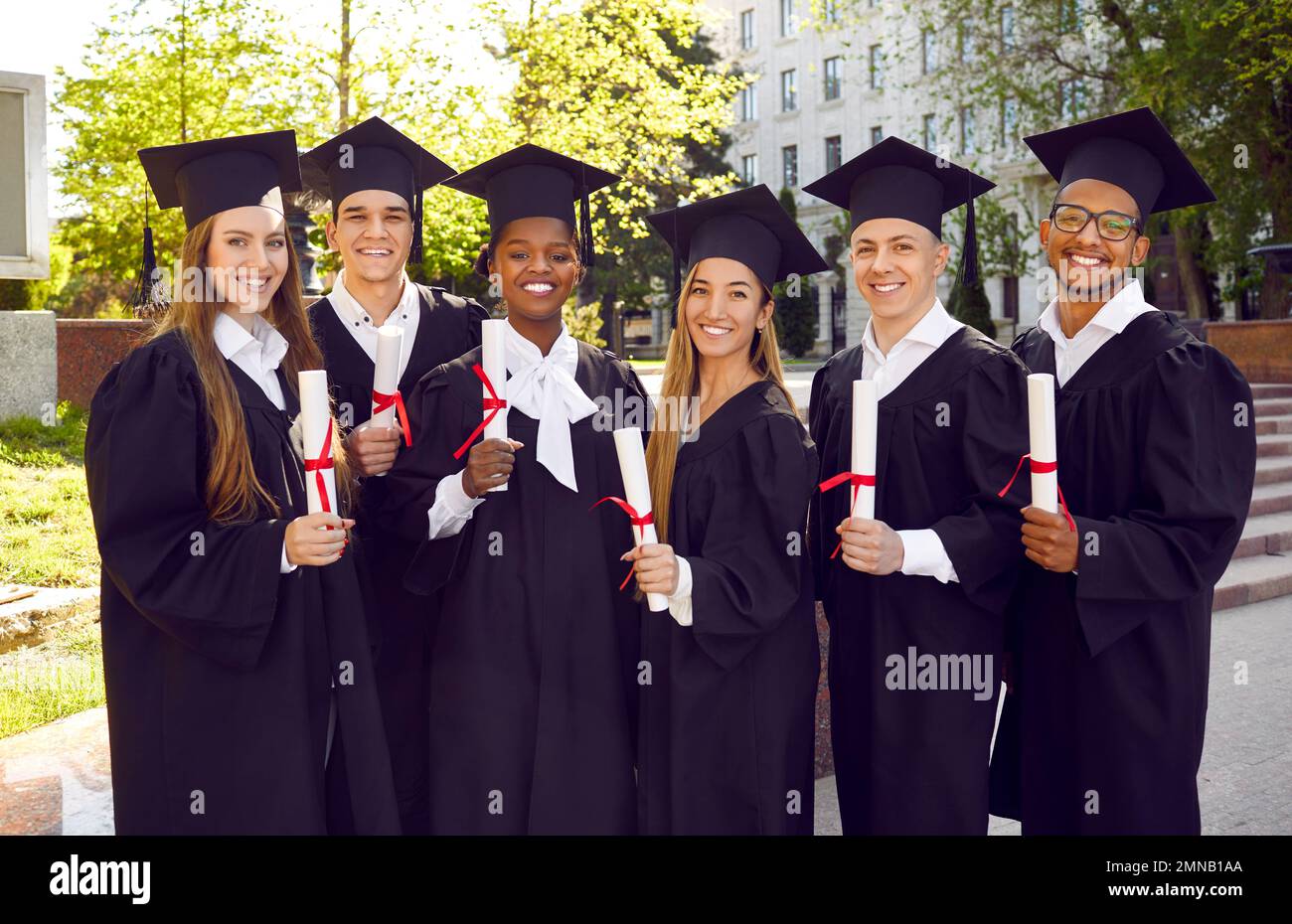Group portrait of happy diverse university students in caps and gowns ...