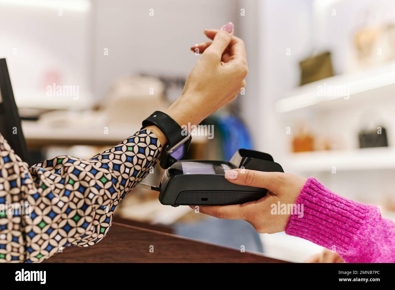 Side view close up of young woman paying via smartwatch in boutique or ...