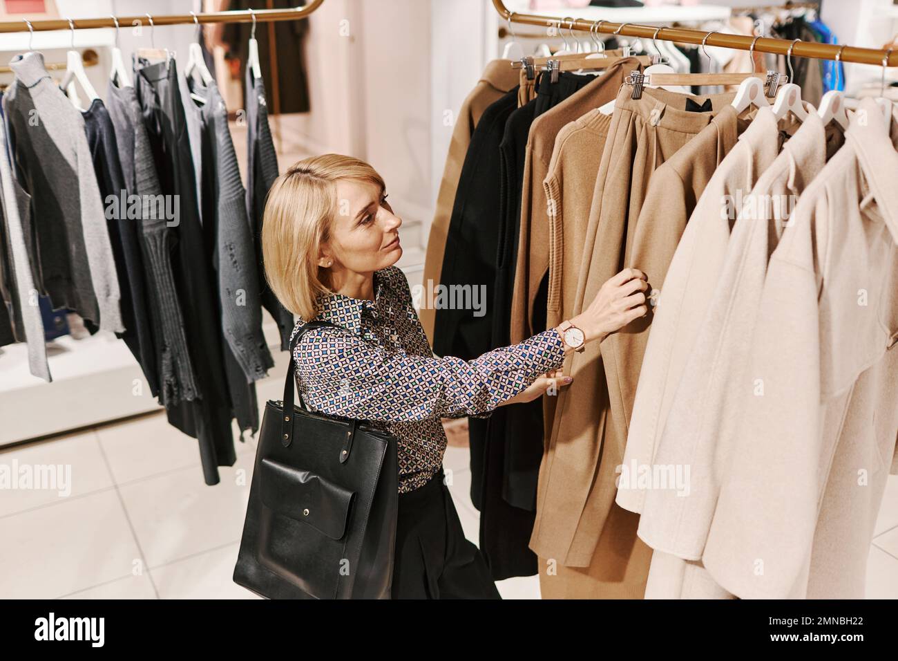Side view portrait of elegant young woman browsing clothes on racks in ...
