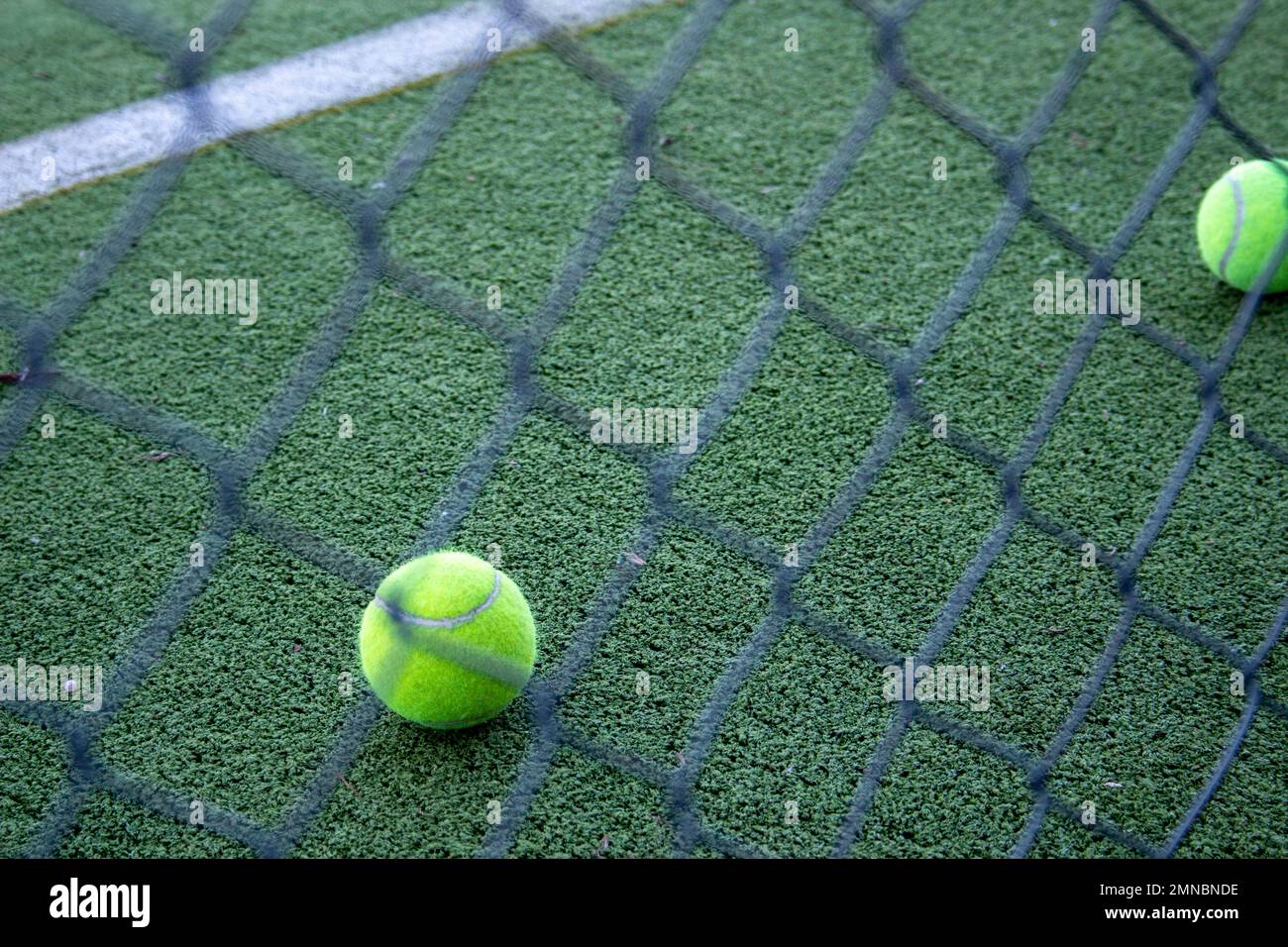 tennis balls on an artificial grass paddle court seen behind a fence ...