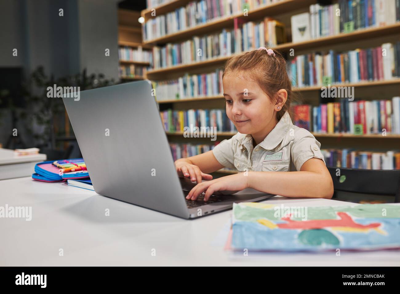 Positively engaged student doing her homework using laptop in after ...