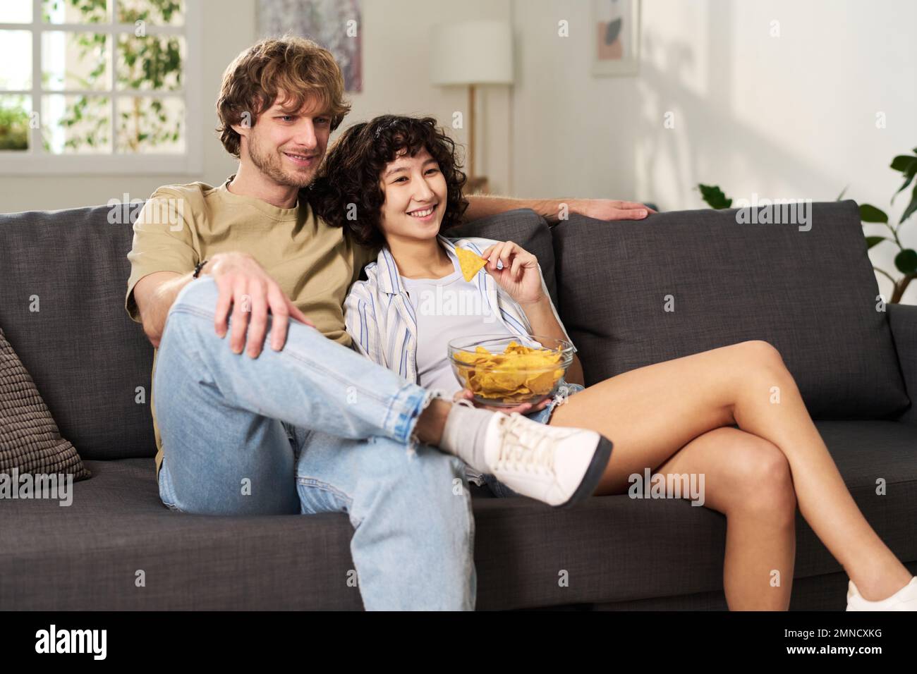 Happy young couple in casualwear relaxing on couch and watching funny ...