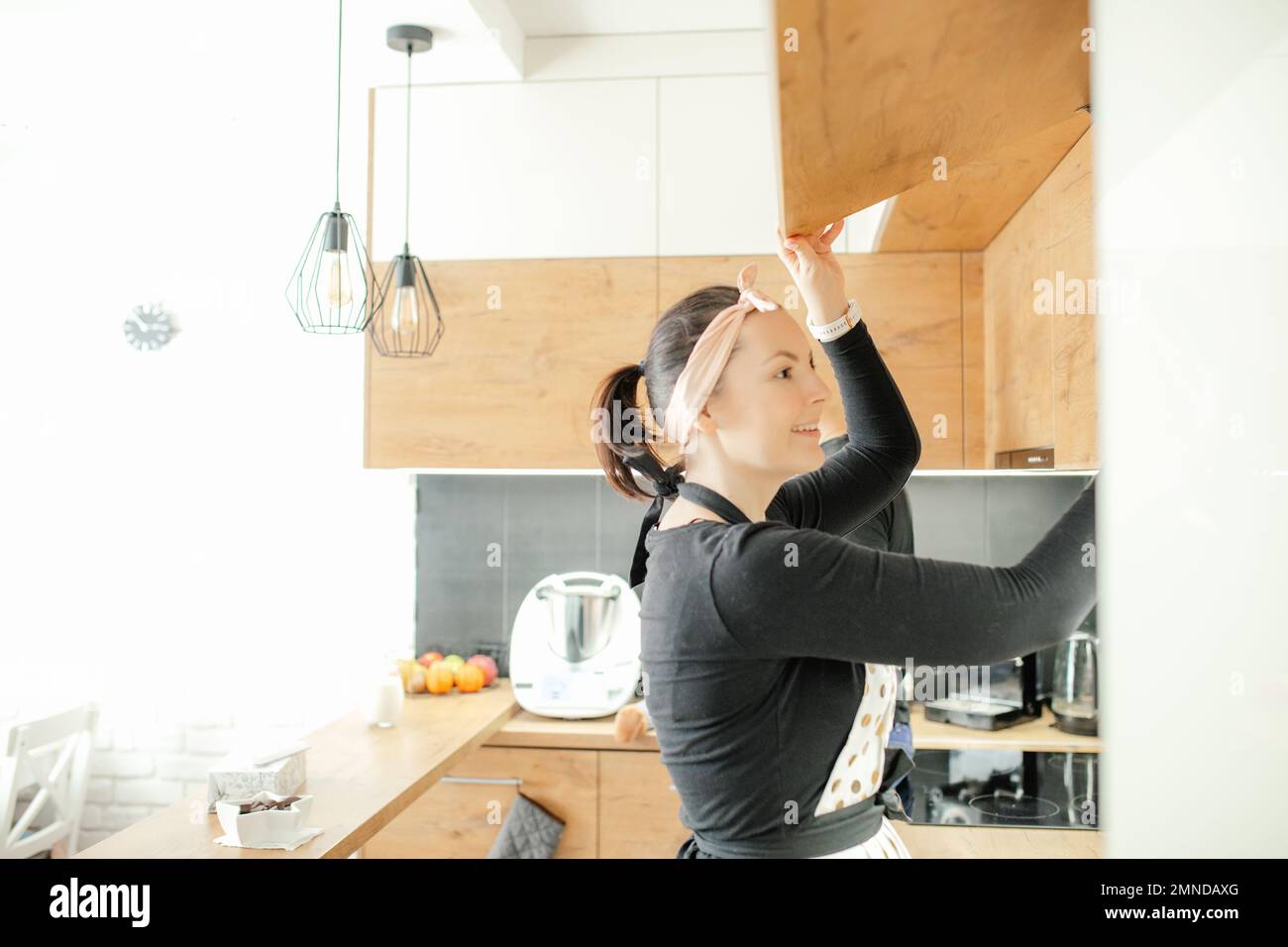 Happy woman open door of upper kitchen cupboard, side view. Housewife ...