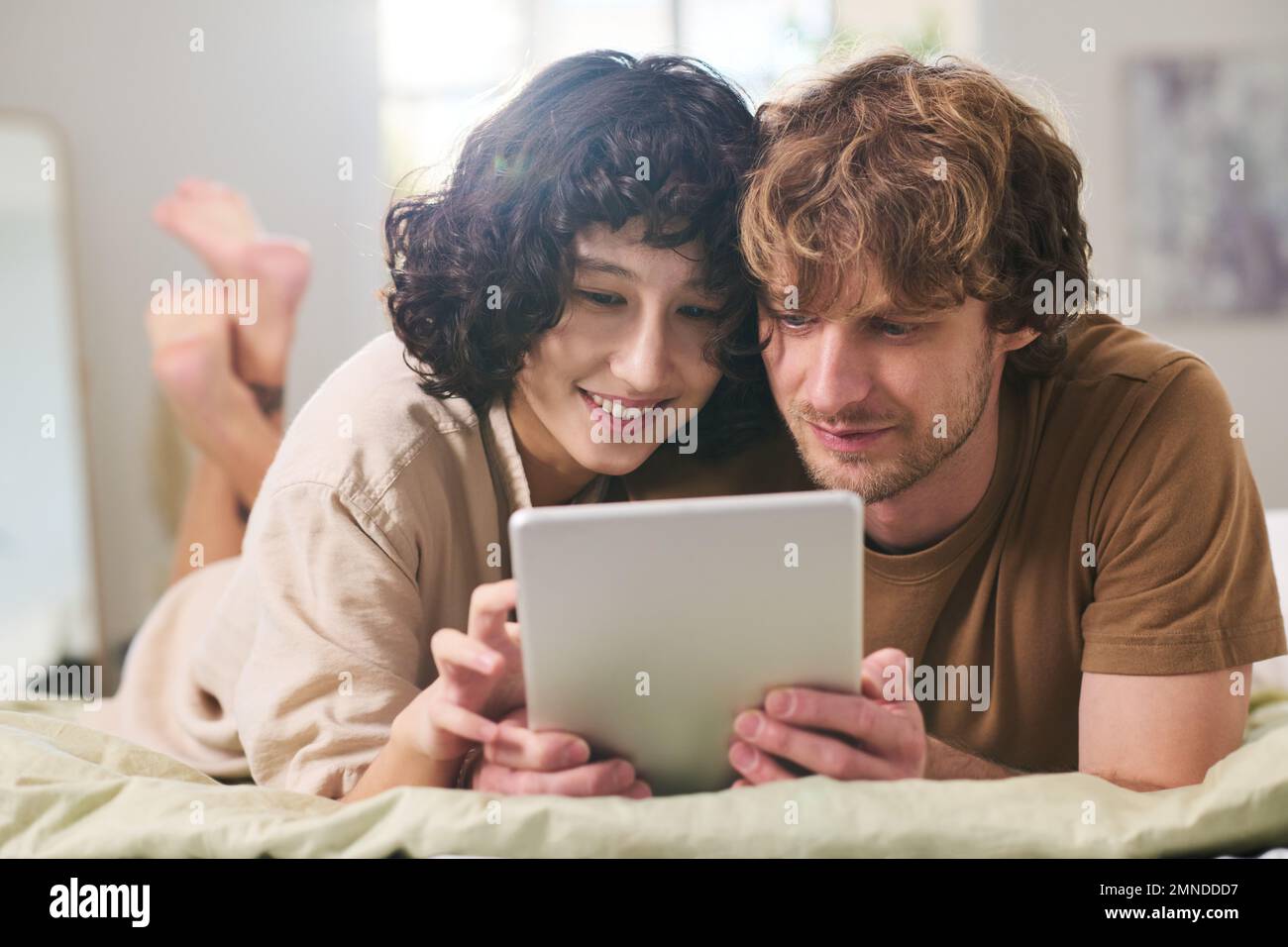 Young affectionate couple looking through online goods on tablet screen ...