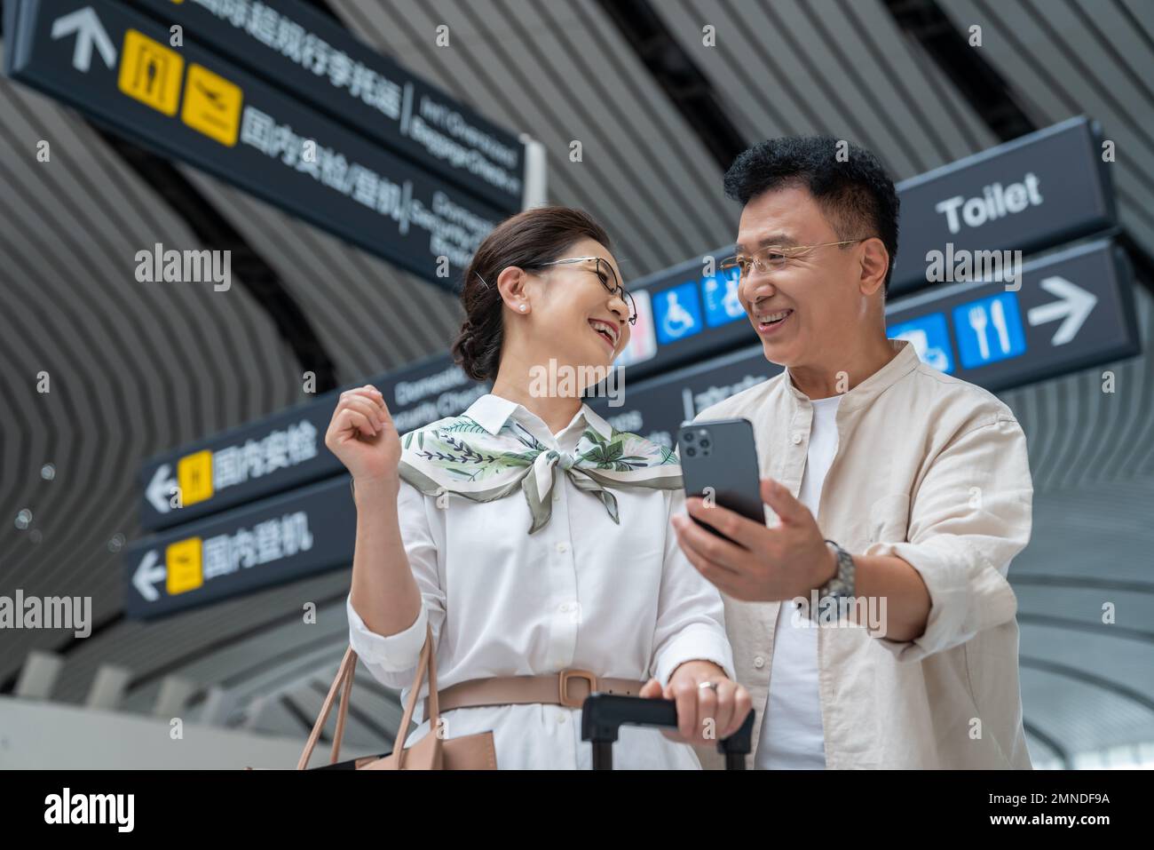 Happy elderly couple using mobile phones at the airport Stock Photo - Alamy