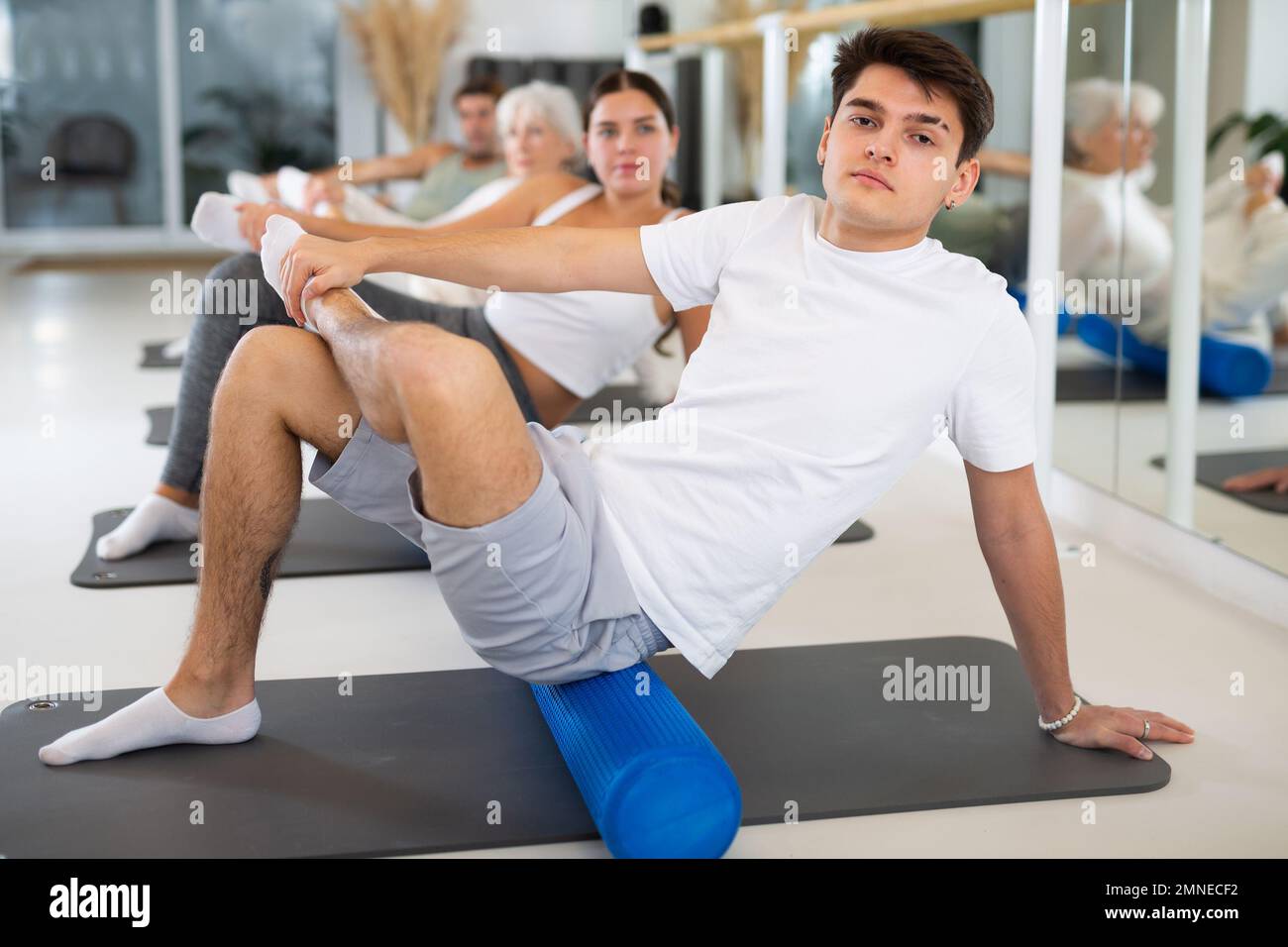 Positive athletic male performing set of exercises with pilates roller ...