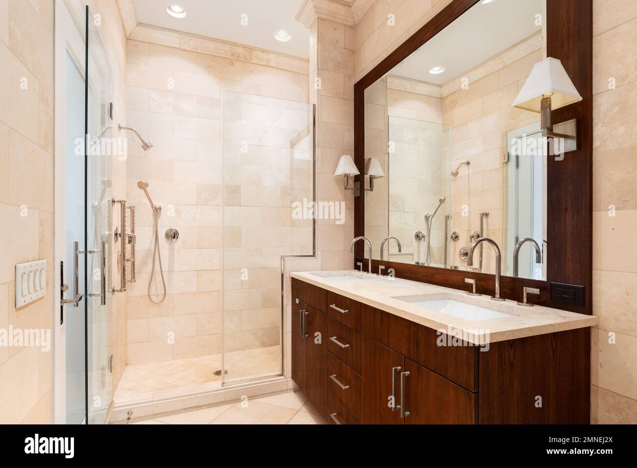 A luxury bathroom with a dark wood cabinet and mirror, tan tiles on the ...