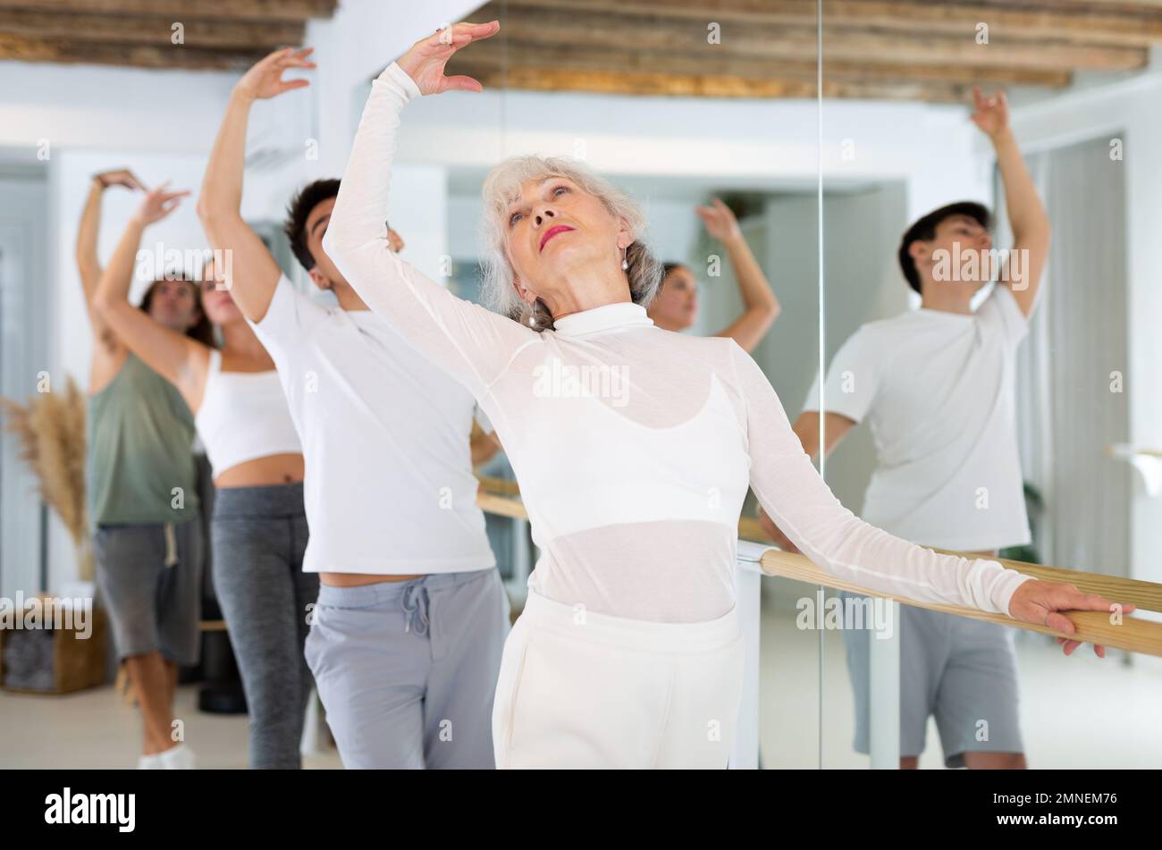 Аged woman choreographer demonstrates ballet stances to students in a ...