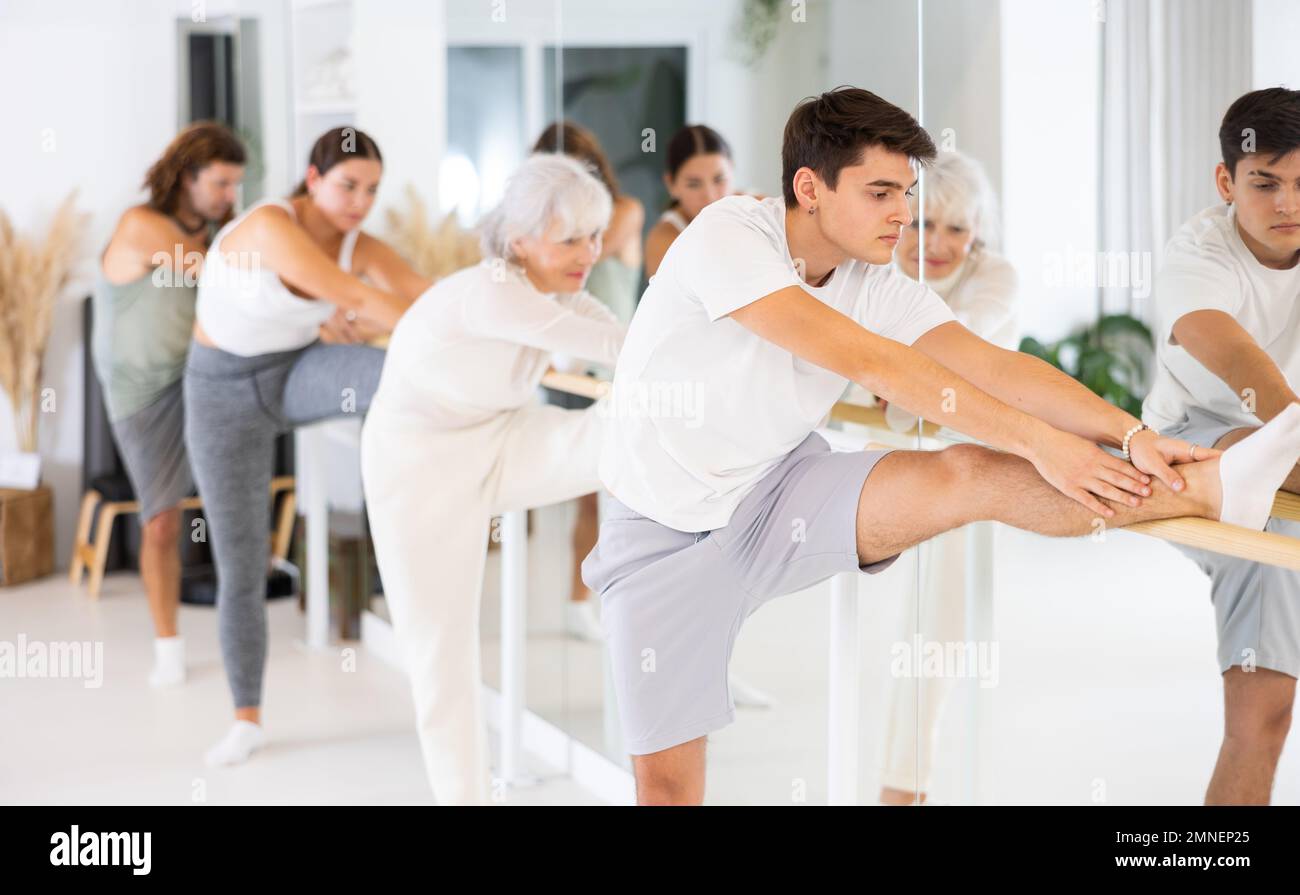 Dancer man exercise stretching on a ballet barre at a group training ...