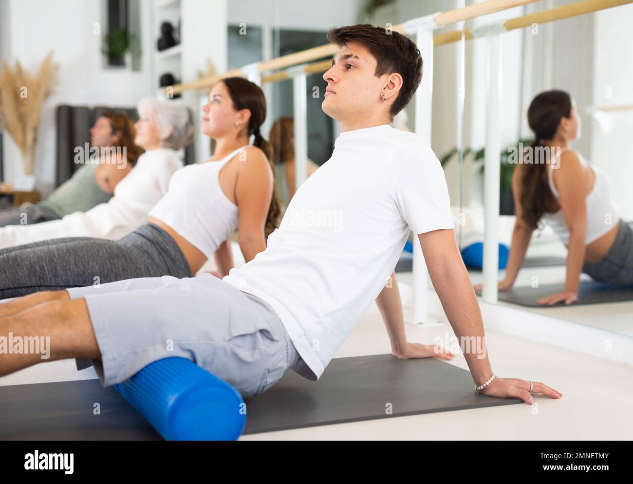 Positive athletic male performing set of exercises with pilates roller ...