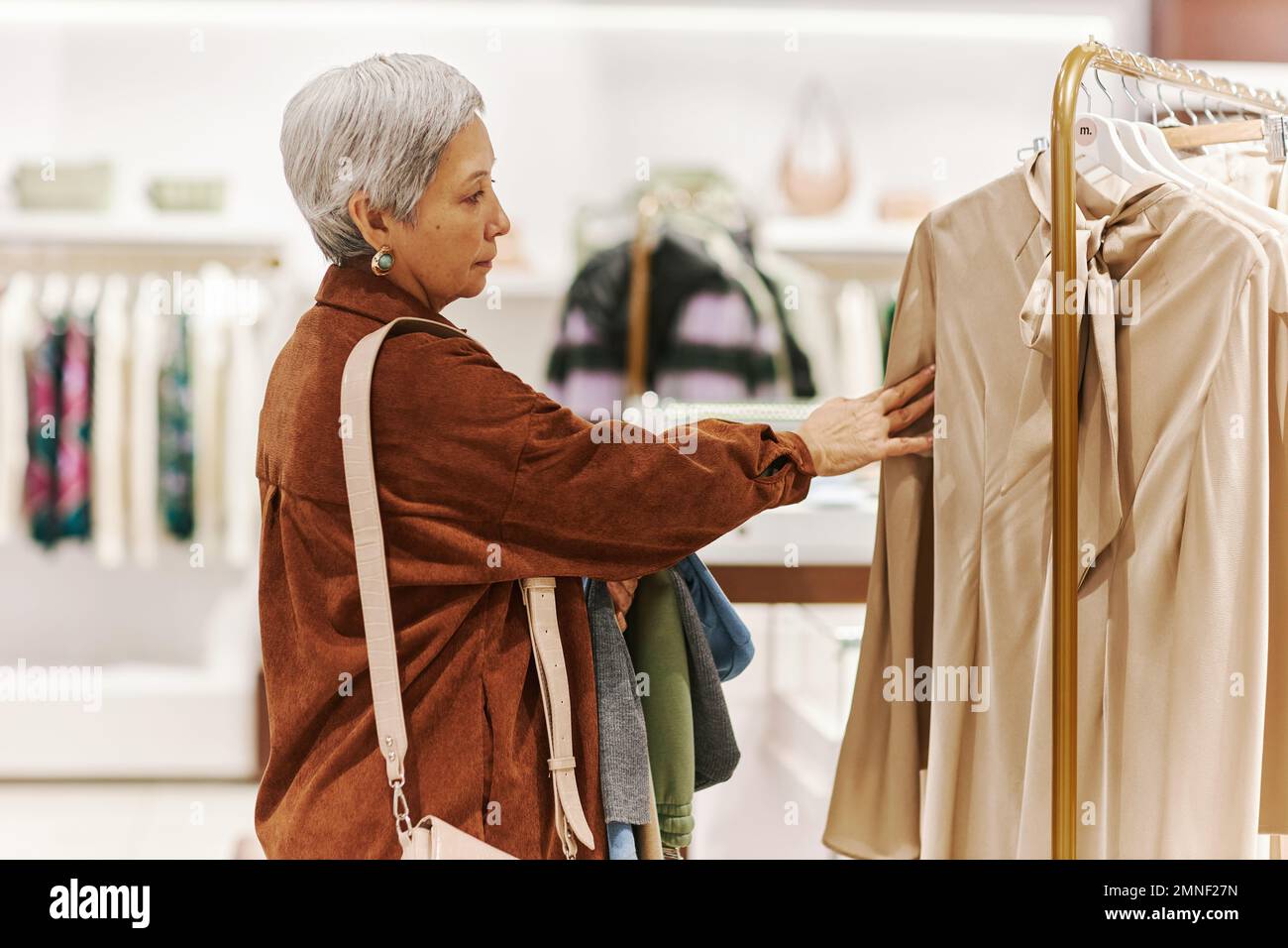Side view of senior woman browsing clothes on racks in luxury boutique ...