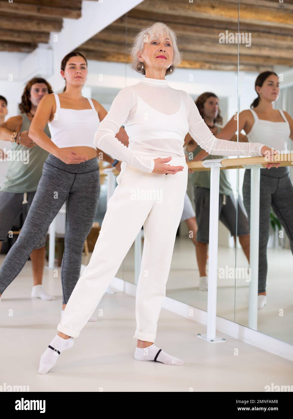 Аged woman choreographer demonstrates ballet stances to students in a ...
