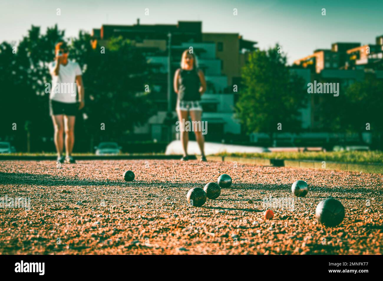Two women playing petanque (boule) in the late afternoon summer sun ...