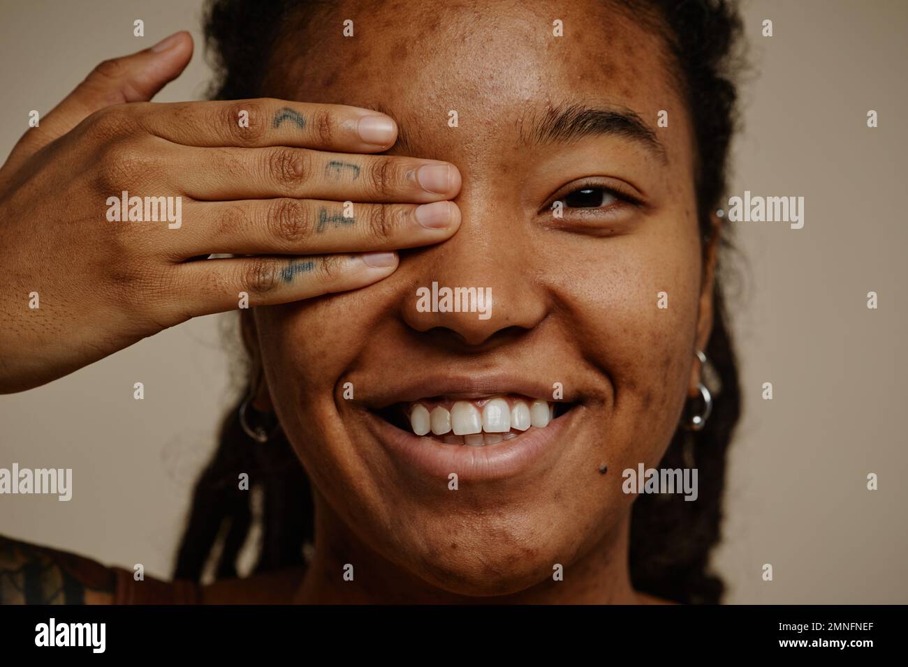 Close up portrait of ethnic young woman smiling candidly with one eye ...