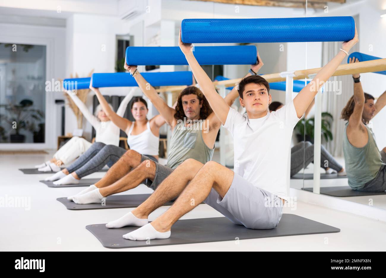 Men and women practicing pilates with roller on gray mat in gym room ...