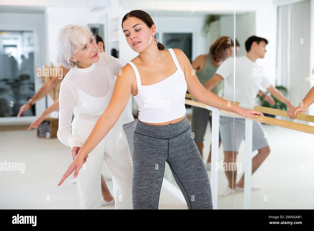 Аged woman choreographer adjusting young female student pose in a ...