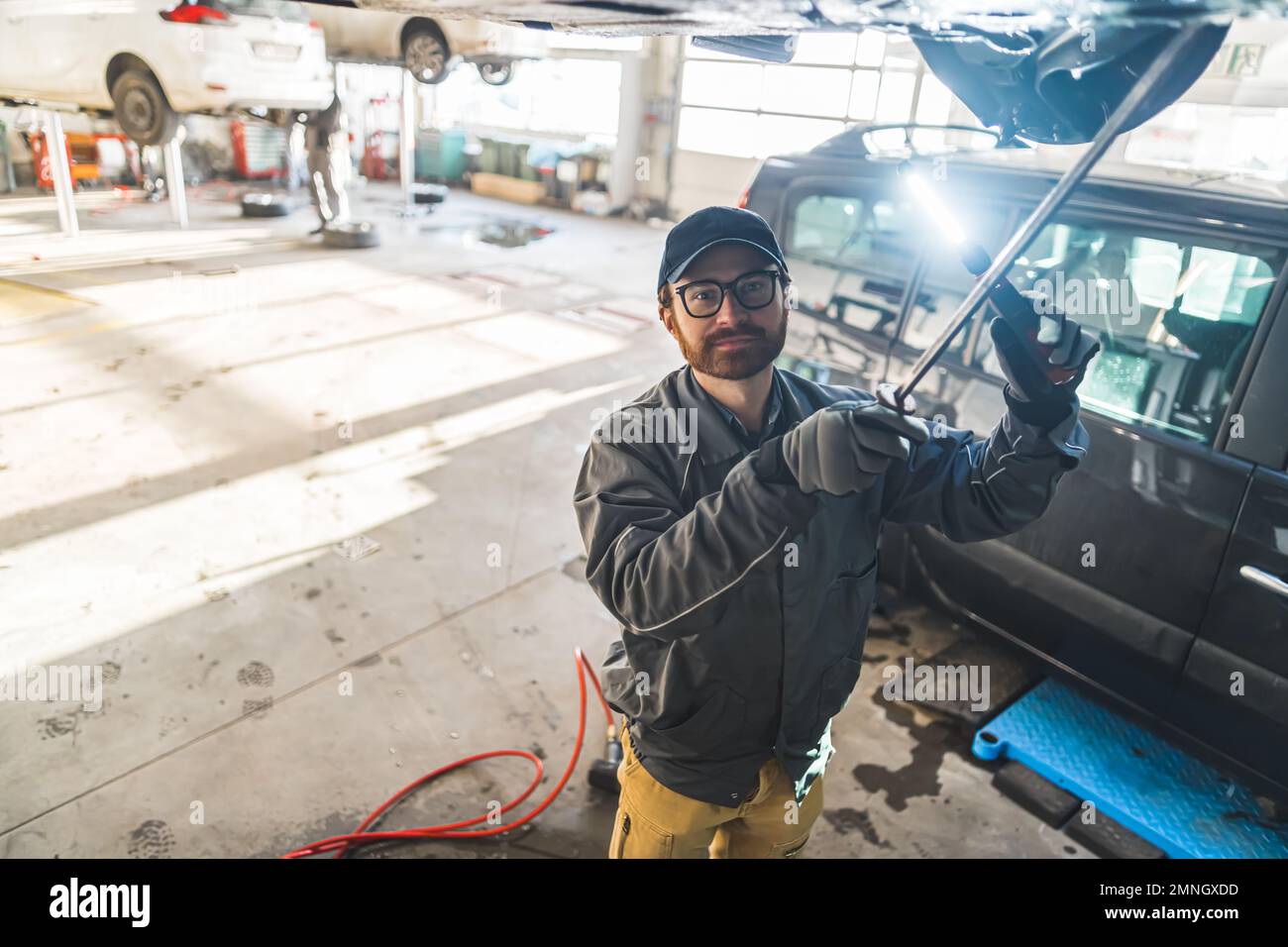 Mechanic with an LED light inspecting a car on a lift in a car repair station. High-quality ...