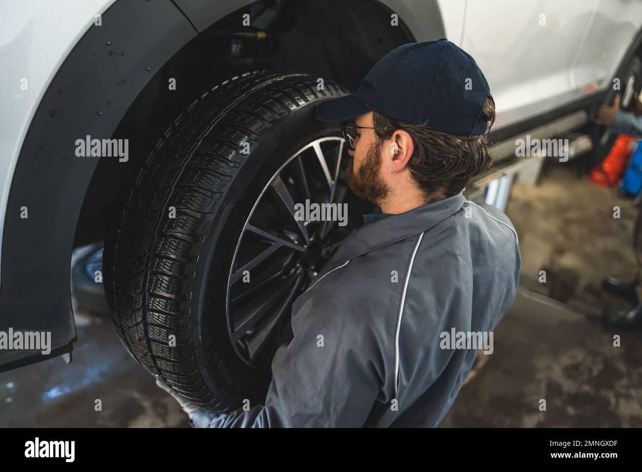 Car mechanic changing wheels of a lifted white car in a repair service ...