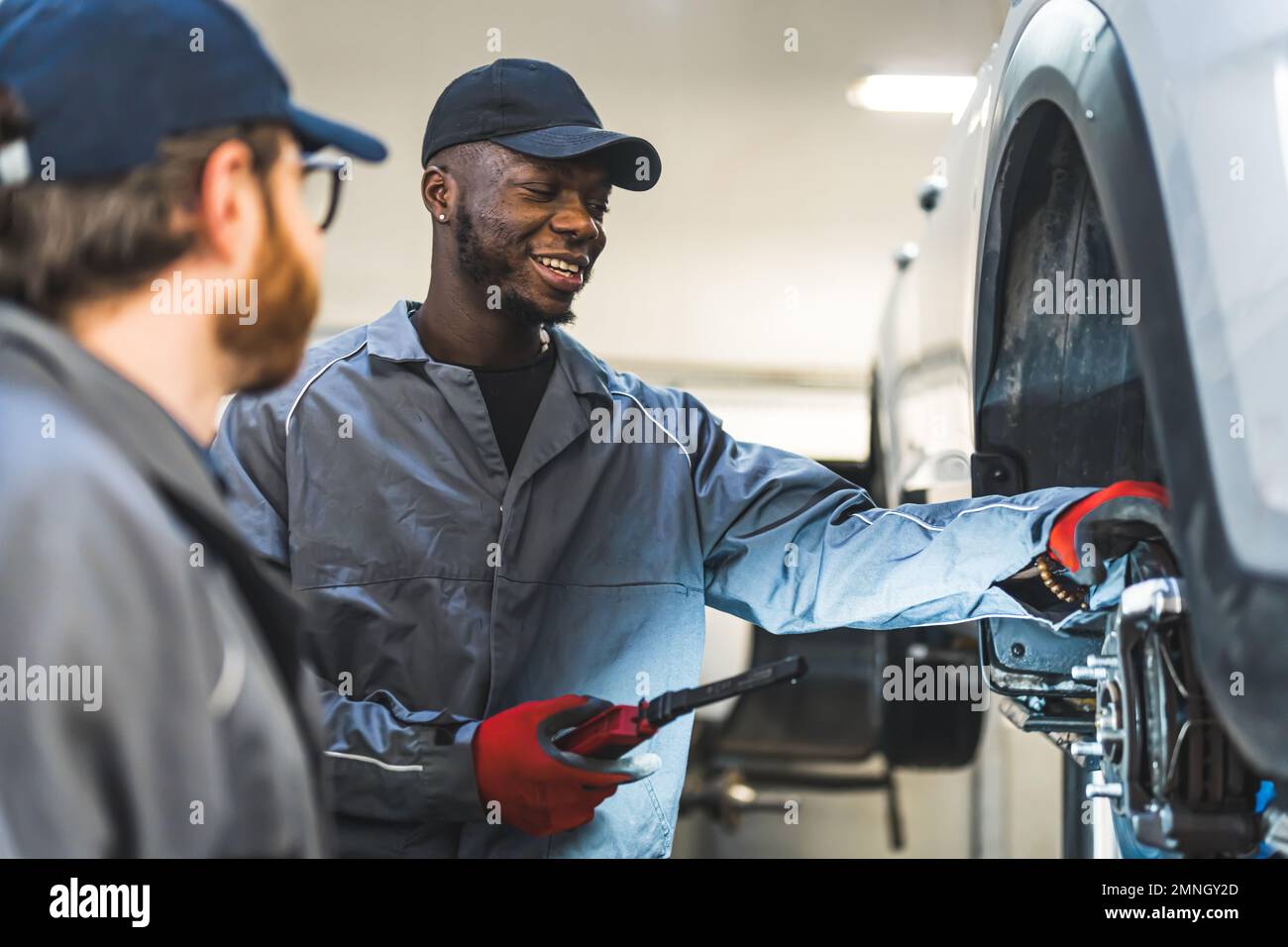Mechanic wearing uniform fixing car tyres using an air wrench in a car ...