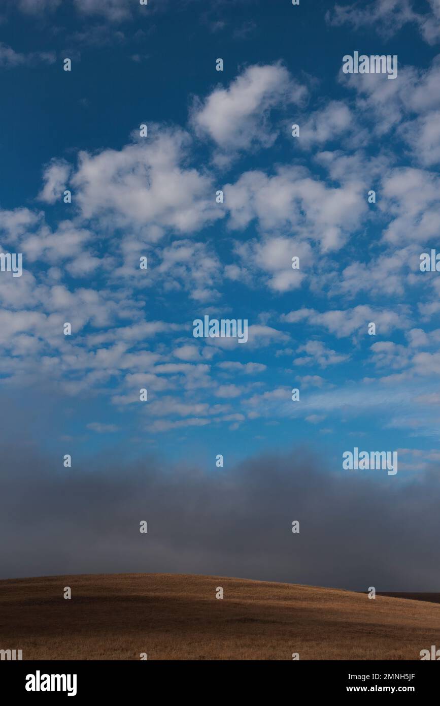 Sun beam across a prairie hillside, blue sky dotted with white clouds ...