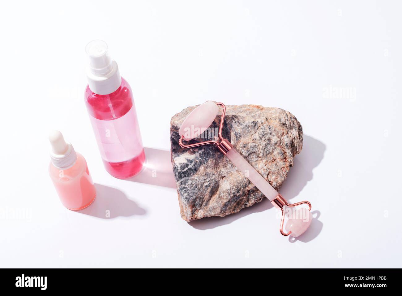 Pink cosmetic bottles and rose quartz crystal facial roller on natural ...