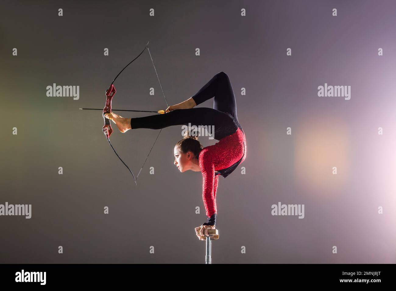 Young acrobat performing with archery bow on gymnastics bar Stock Photo ...
