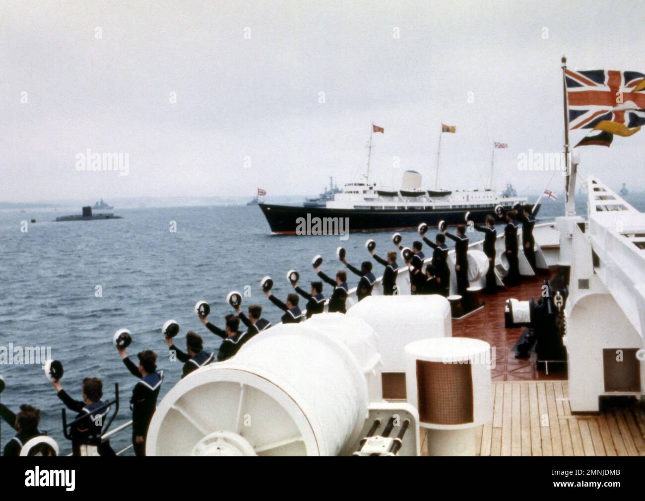 Sailors aboard HMS Hermes raise their hats in salute as the royal yacht Britannia passes by ...