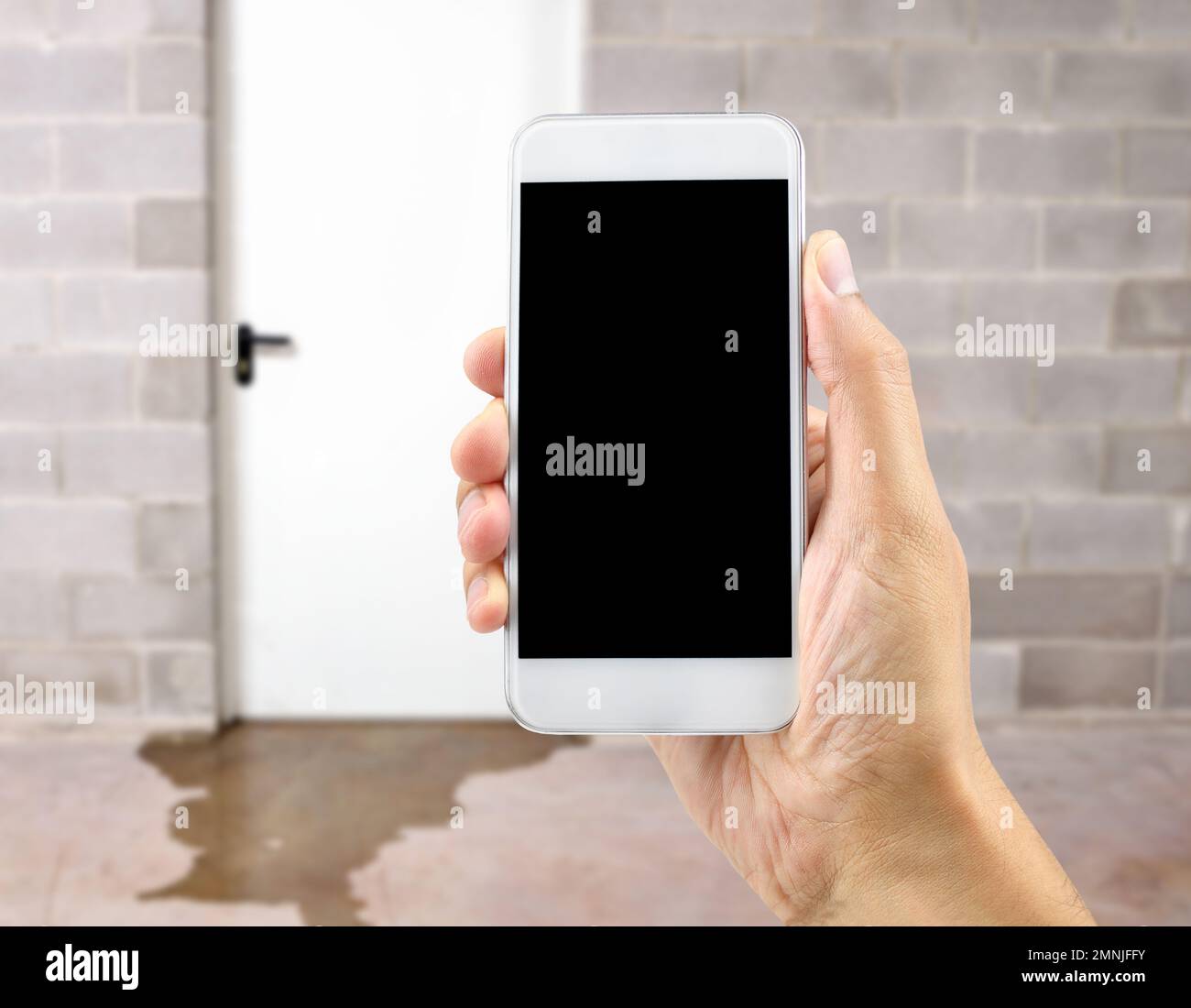 A hand holding up a smart phone with water damage in basement caused by ...