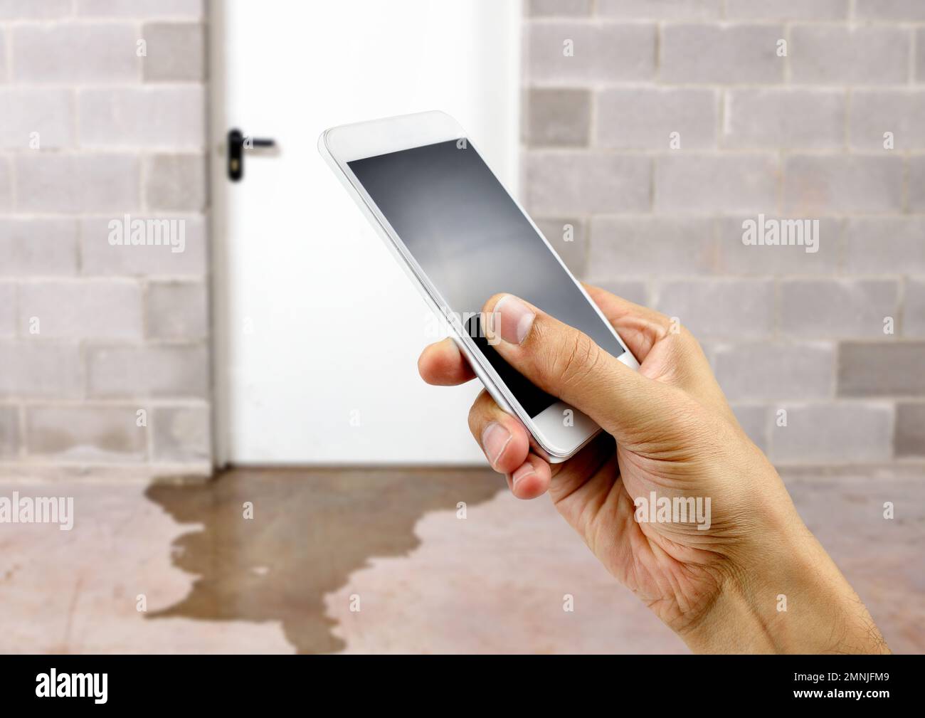 A hand holding up a smart phone with water damage in basement caused by ...