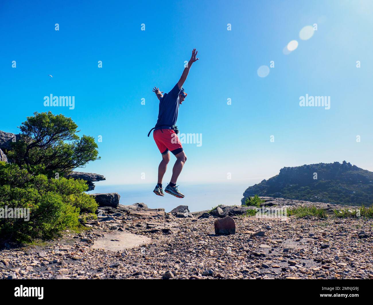 South Africa, Western Cape, Cape Town, Man jumping on cliff with arms ...