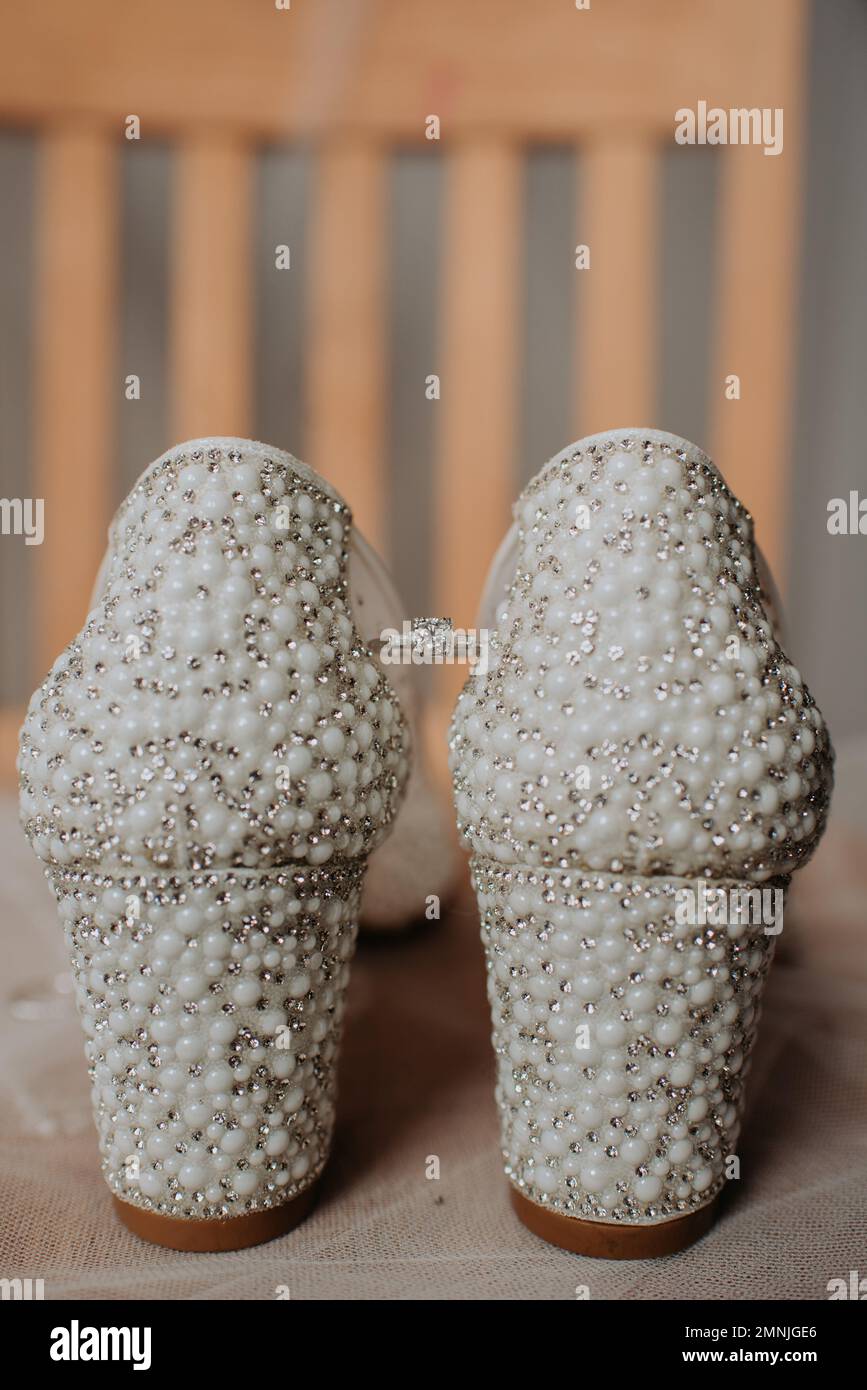 A simple engagement ring in between a pair of wedding shoes covered in ...
